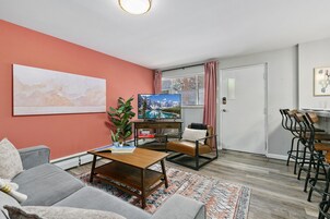Sala de estar com sofá, mesa de centro, televisão e um espaço de jantar com cadeiras.