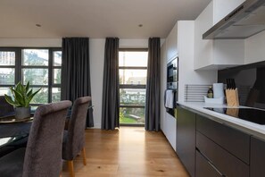 Uma cozinha moderna com forno embutido, espaço de jantar com mesa e cadeiras, e grandes janelas com cortinas.