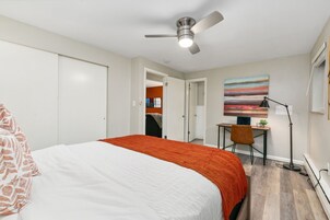 Quarto com cama, escrivaninha, cadeira, ventilador de teto e pintura na parede.