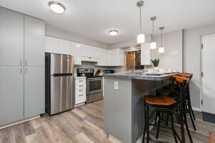 Uma cozinha moderna com eletrodomésticos de aço inoxidável, uma ilha central com banquetas e iluminação pendente.