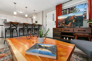 Uma sala de estar moderna com uma mesa de centro de madeira, um livro intitulado "Colorado: An Historical Atlas" e uma grande televisão de tela plana exibindo uma paisagem de montanhas.