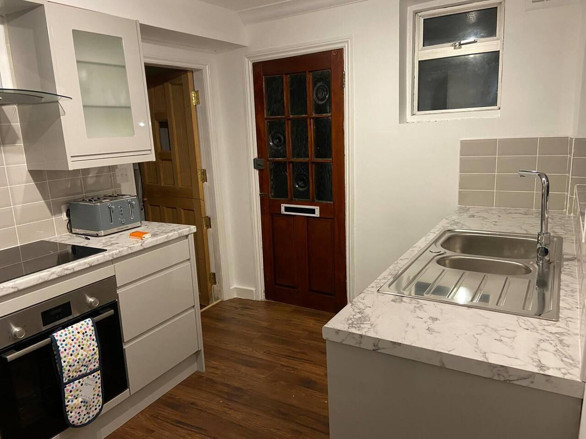 Uma cozinha com armários brancos, uma porta de madeira, uma janela e uma pia.