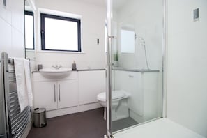 Uma casa de banho moderna com cabine de duche em vidro, lavatório branco e sanita.