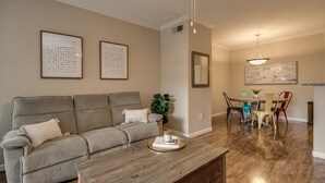 Uma sala de estar com um sofá cinza, uma mesa de centro de madeira e um espaço de jantar com mesa e cadeiras de madeira.