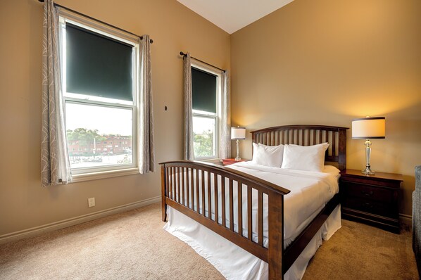Quarto com cama grande, duas mesas de cabeceira, janela com cortinas e vista exterior.