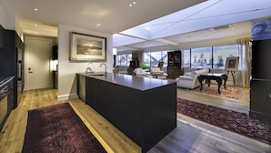 Uma cozinha moderna com uma ilha grande, uma sala de jantar com mesa e cadeiras, e uma sala de estar com sofá e um quadro na parede.