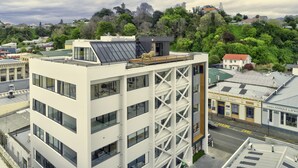 Um edifício moderno com vários andares, janelas amplas e um terraço com painéis solares.