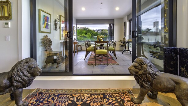 Decoração moderna com porta de vidro que dá para uma sala de jantar, uma estátua de leão e vista para o verde lá fora.