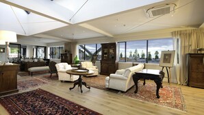 Uma sala de estar ampla com teto alto, grandes janelas com vista para árvores e diversos móveis e objetos decorativos.