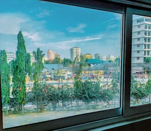 Vista pela janela de um horizonte urbano com edifícios, árvores e céu claro.