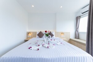 Quarto de hotel com uma cama bem arrumada, janela com cortinas, ar-condicionado fixado na parede e mesa de cabeceira com abajur.