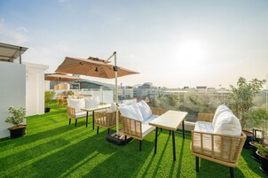 Terraço no telhado com grama sintética verde, mobiliário de vime e plantas em vasos.