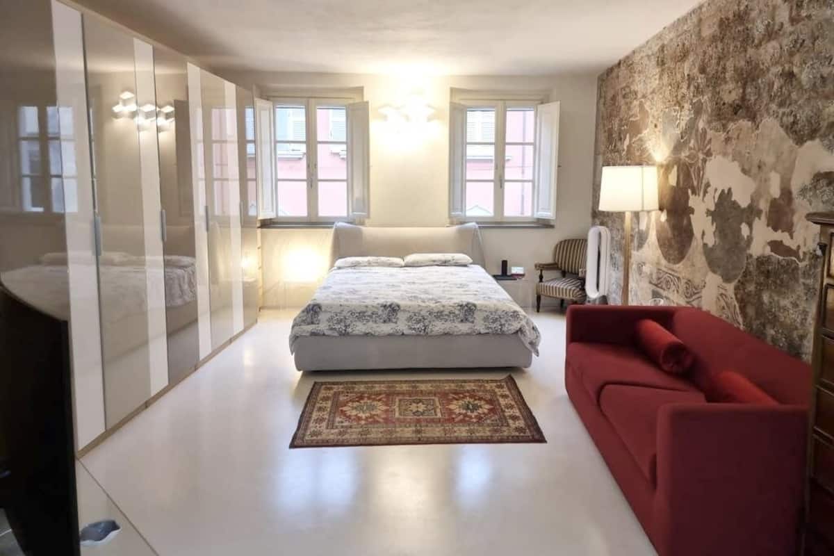 Quarto com uma cama grande, um sofá vermelho, um tapete estampado e uma parede com design texturizado.