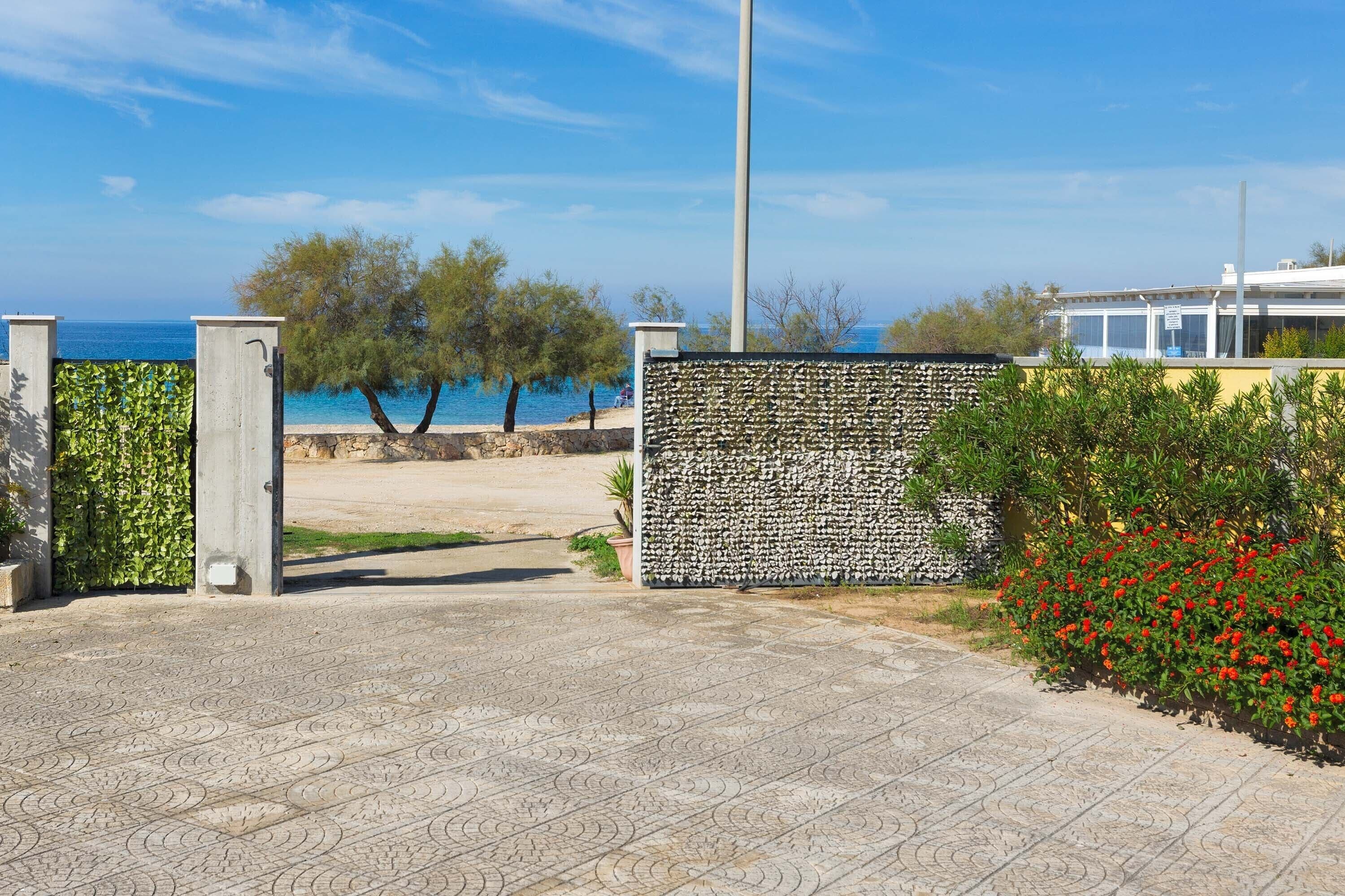 Uma entrada pavimentada com um muro decorativo, um portão e vista para o mar.