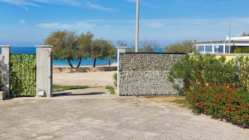 Uma entrada pavimentada com um muro decorativo, um portão e vista para o mar.
