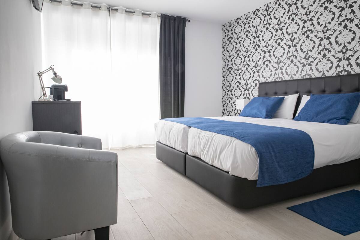 Quarto moderno com uma cama, uma cadeira, uma escrivaninha com abajur e papel de parede estampado.