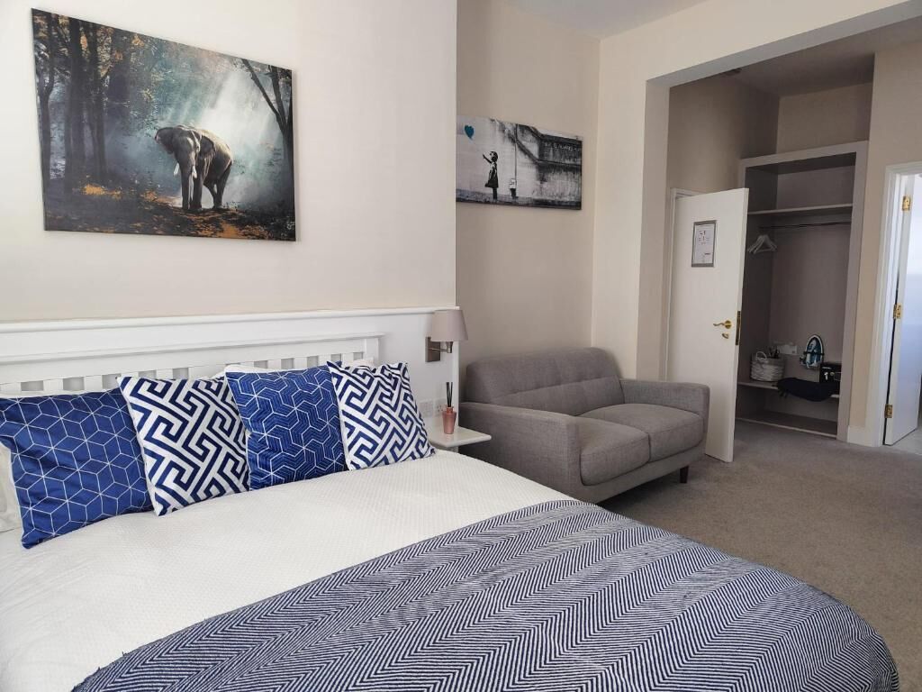 Quarto com cama, sofá cinza, guarda-roupa e duas pinturas na parede.
