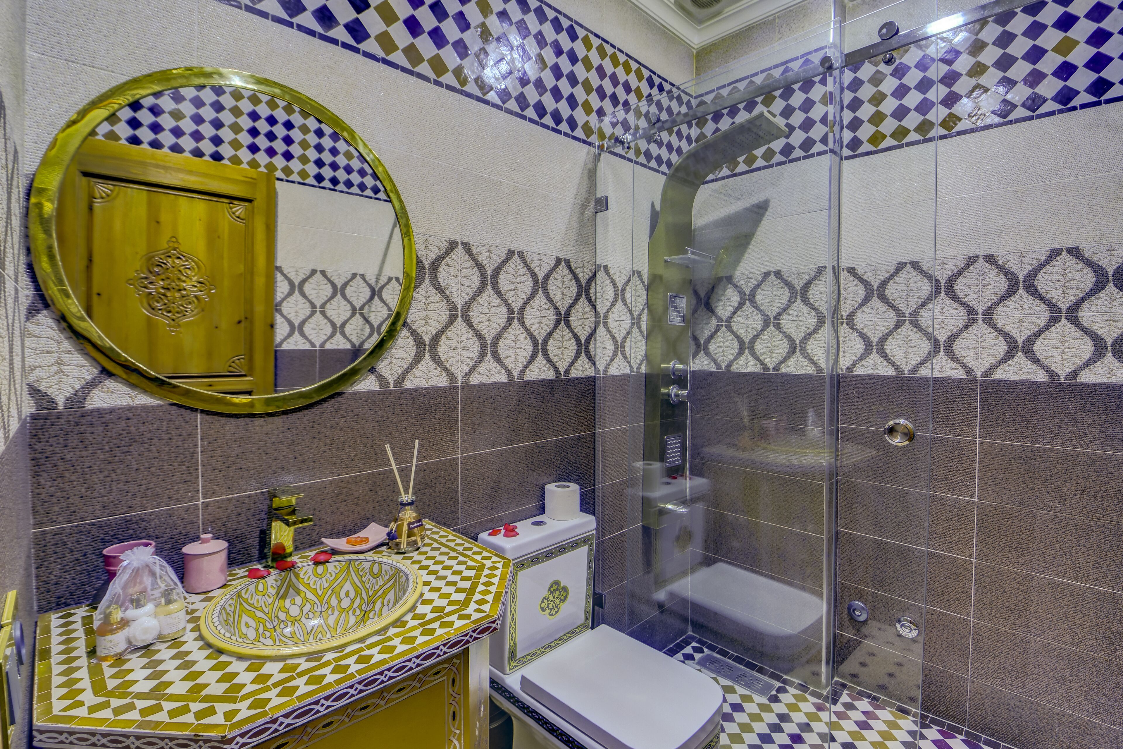 Casa de banho com painel de azulejos xadrez, espelho redondo, sanita e cabine de chuveiro em vidro.