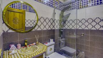 Casa de banho com painel de azulejos xadrez, espelho redondo, sanita e cabine de chuveiro em vidro.