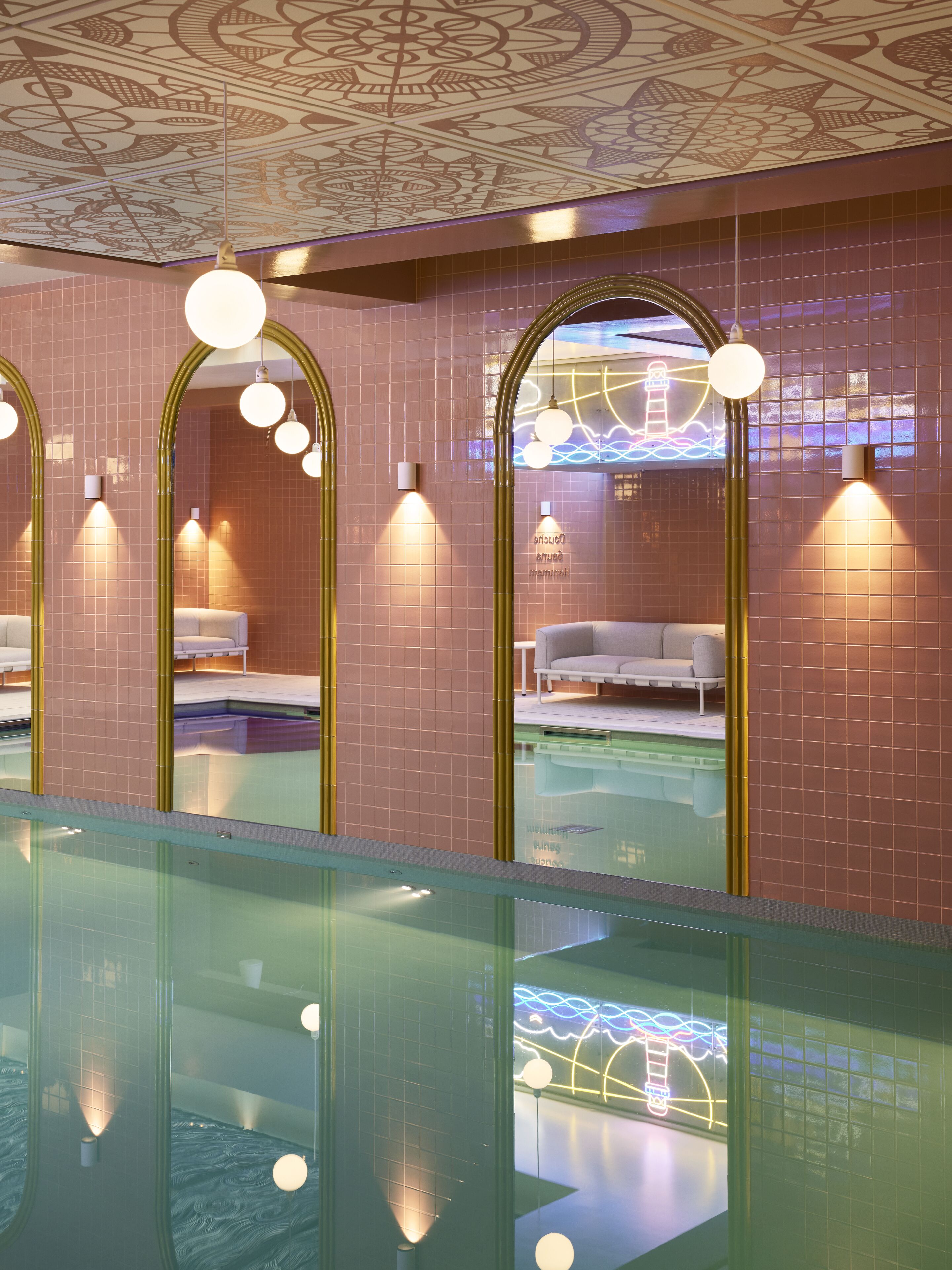 Uma piscina interior moderna com paredes de vidro transparente, teto estampado e luminárias contemporâneas.