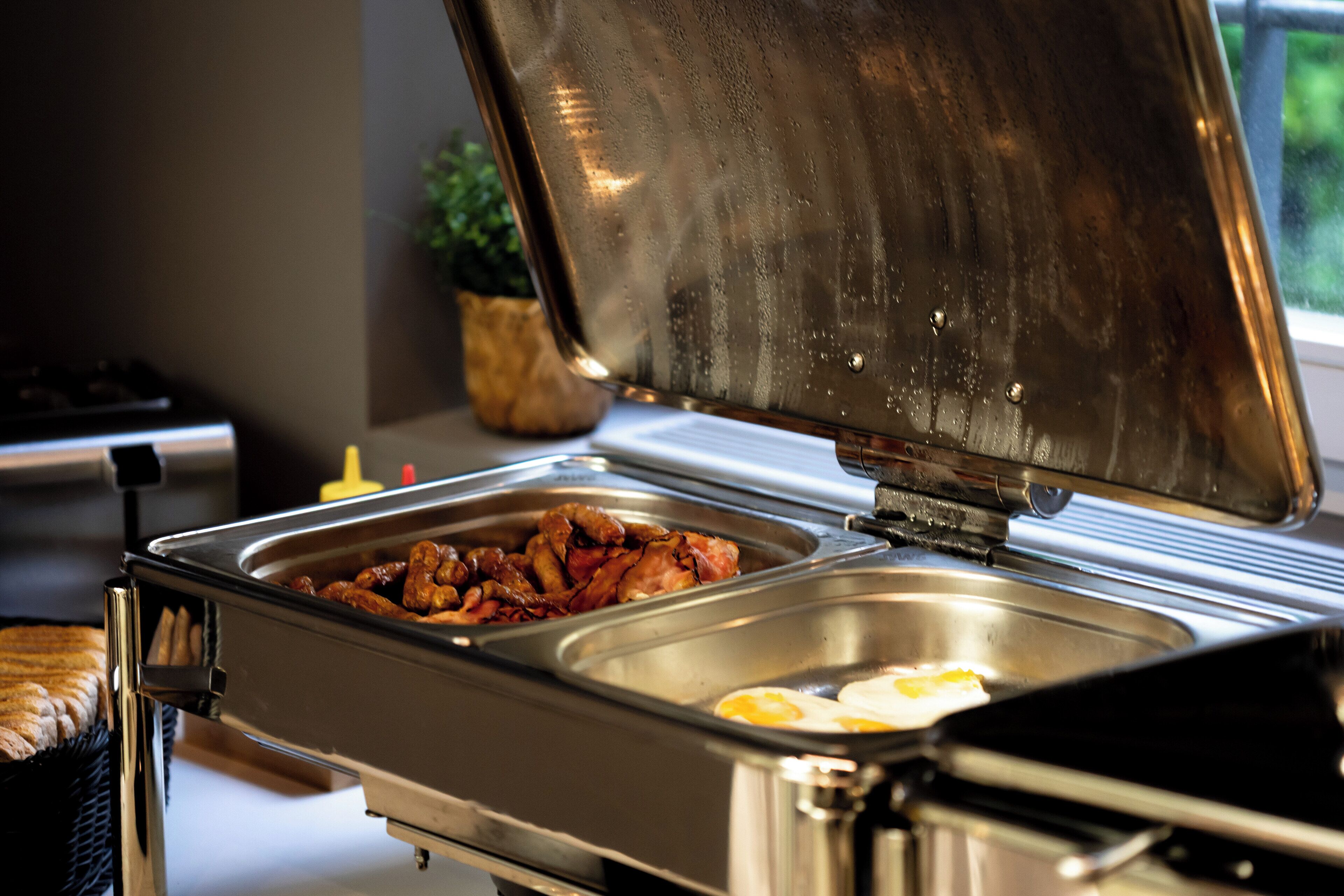 Buffet com diversos alimentos e uma planta ao fundo.