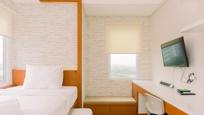 Quarto de hotel com cama, escrivaninha com cadeira, televisão e janela com vista.