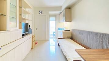 Quarto de hotel compacto com cozinha compacta, uma cama, televisão e banheiro com chuveiro.