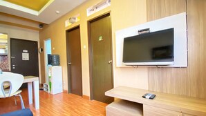 Quarto de hotel com piso de madeira, televisão fixada na parede, uma secretária pequena e uma cadeira.