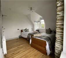 Quarto com duas camas, piso de madeira, teto inclinado e uma janela.