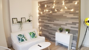 Uma sala de estar moderna com um sofá branco, uma mesa de centro branca e um console branco com plantas. Há luzes de cordão na parede, um abajur e uma cadeira.