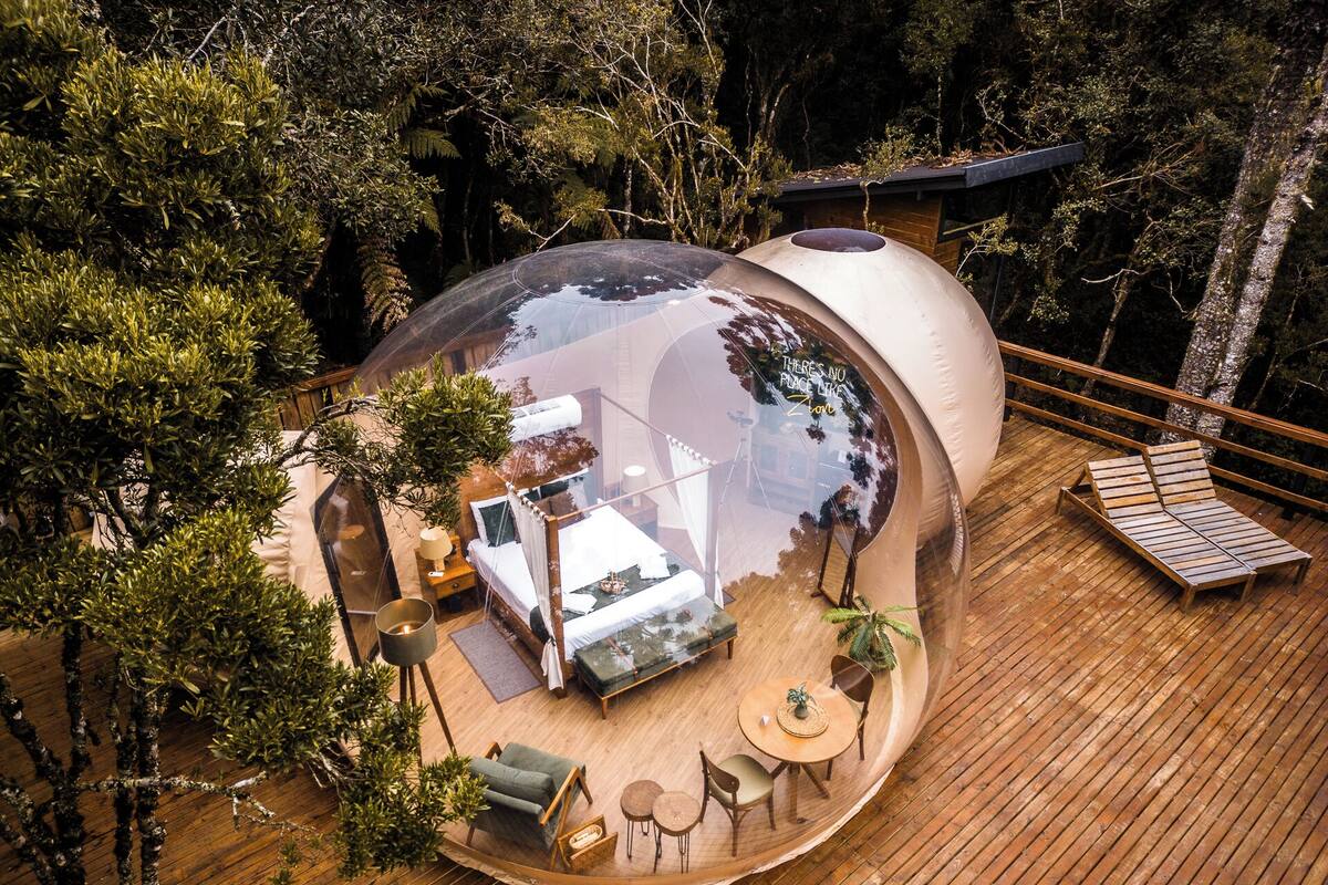 Estrutura em cúpula transparente com cama, área de estar e mesa de jantar.