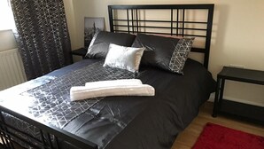 Uma cama bem arrumada, com estrutura de metal preta, colcha estampada e vários travesseiros.