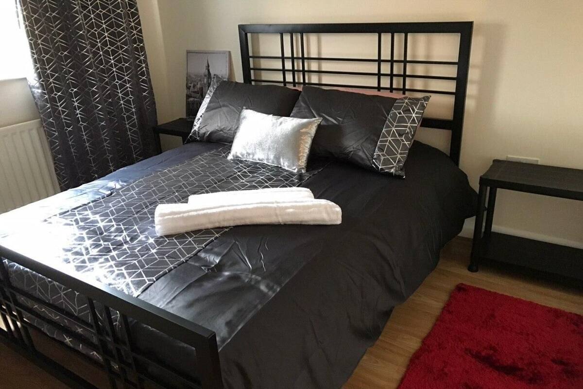 Uma cama bem arrumada, com estrutura de metal preta, colcha estampada e vários travesseiros.