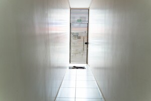 Um corredor com uma porta no final, piso ladrilhado e um portão de metal com uma placa em cima.