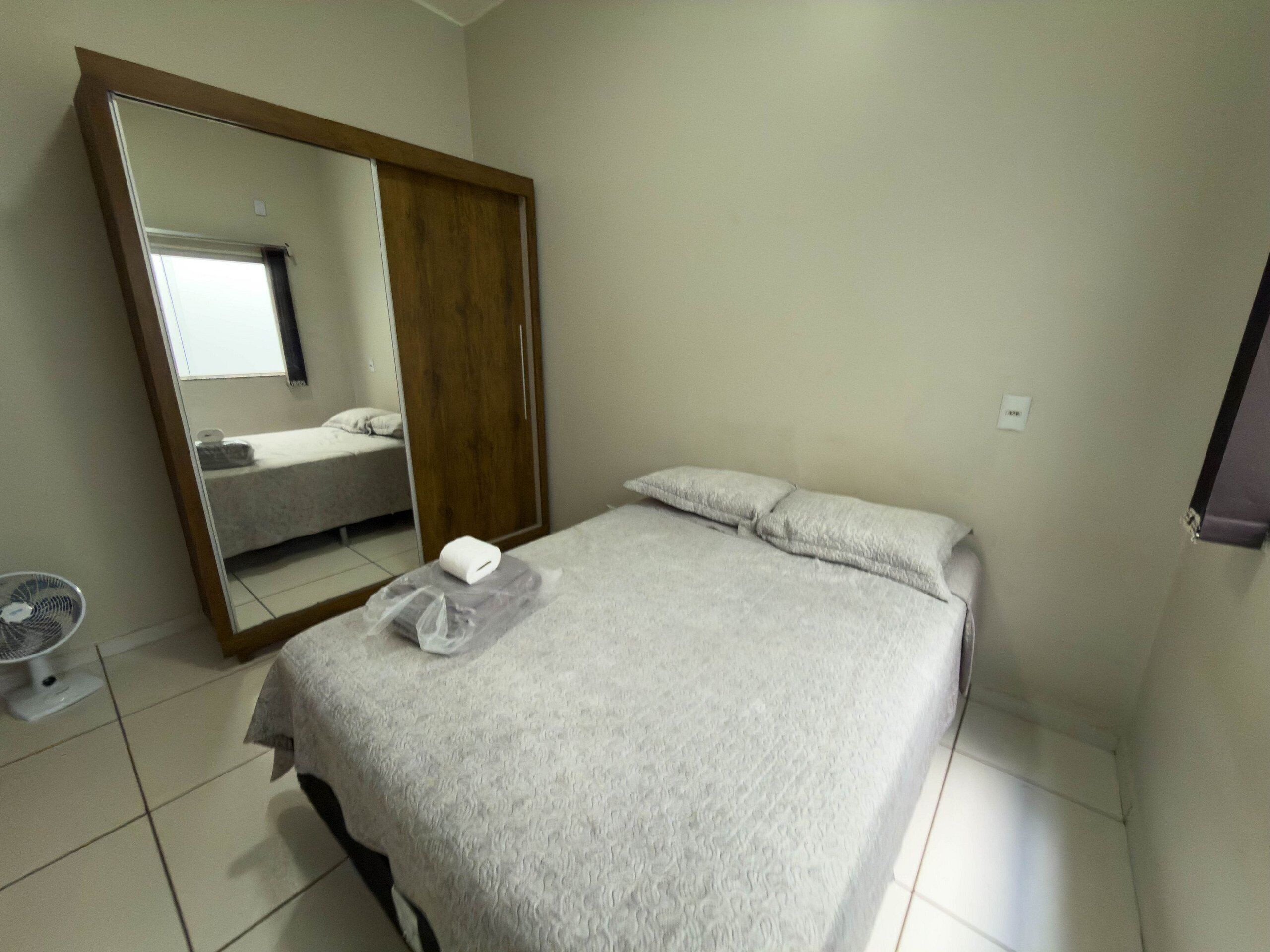 Quarto com cama, espelho, guarda-roupa e ventoinha.