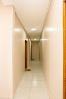 Um corredor estreito, bem iluminado, com chão de azulejos e portas de madeira em ambos os lados.