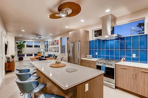 Cozinha moderna com ilha central, eletrodomésticos de aço inoxidável e azulejos azuis na parede.