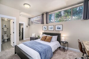 Um quarto com uma cama grande, mesas de cabeceira, uma escrivaninha e uma janela com cortinas.