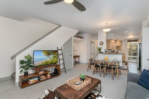 Uma sala de estar moderna com uma televisão de tela plana, uma mesa de centro de madeira e uma área de jantar com mesa e cadeiras de vidro.