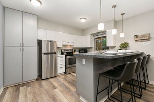 Uma cozinha moderna com eletrodomésticos de aço inoxidável, uma ilha central com banquetas e iluminação pendente.