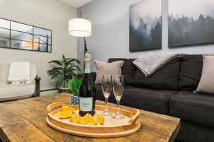 Sala de estar com mesa de centro de madeira, garrafa de vinho, copos e fatias de laranja.