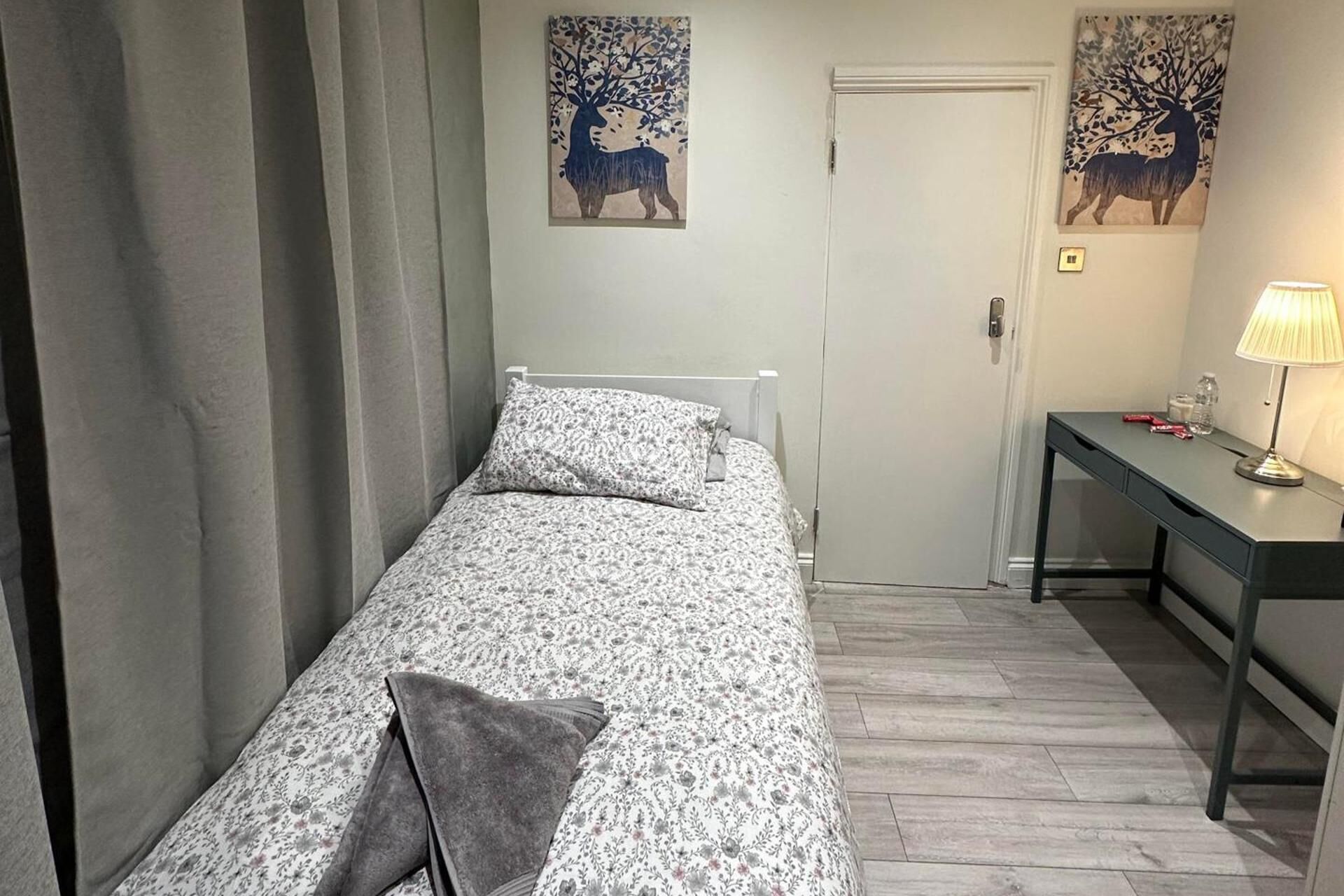 Quarto com uma cama, uma escrivaninha, uma luminária e duas obras de arte na parede retratando veados.