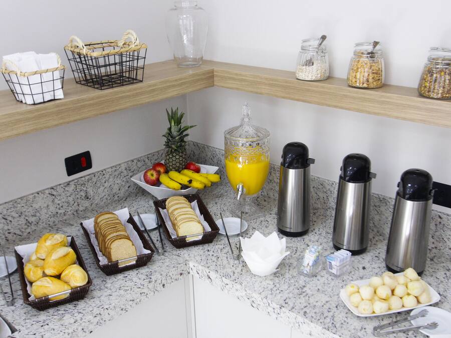 Um buffet de café da manhã com pães, doces, frutas e sucos.