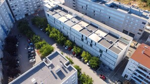 Um edifício de vários andares com telhado plano, diversas varandas e um estacionamento com carros.