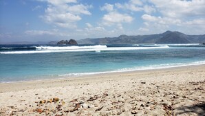 Uma praia com céu claro, ondas e montanhas ao longe.