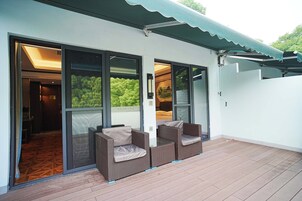 Uma área de estar coberta ao ar livre, com mobiliário de vime e portas de correr que dão para um espaço interior.
