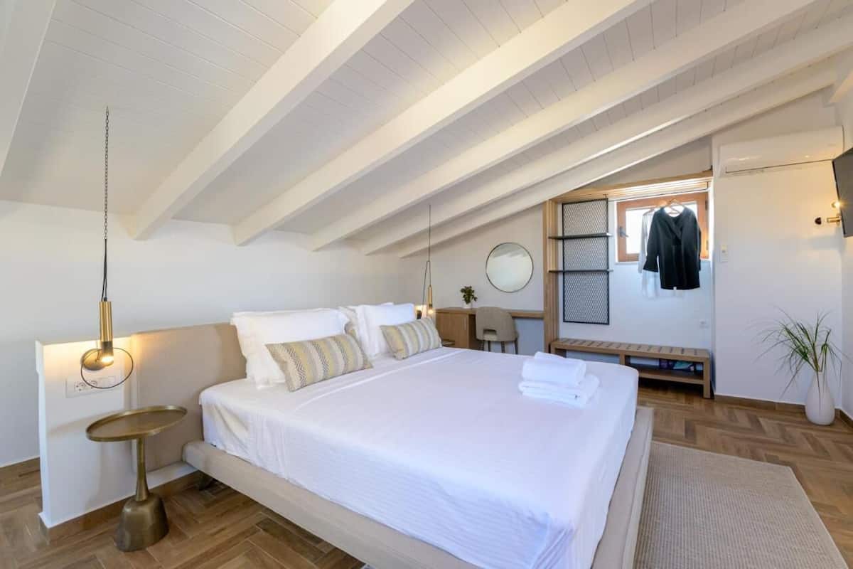 Um quarto com uma cama grande, mesas de cabeceira, um lustre, um espelho redondo e uma pequena escrivaninha com cadeira.
