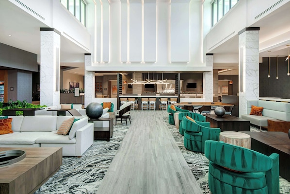 Um hall amplo com uma passarela central, áreas de estar e uma mesa de recepção.