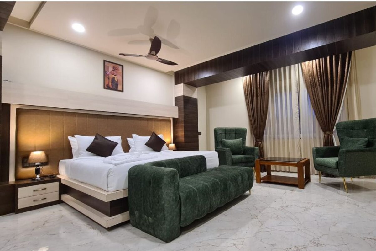 Um quarto moderno com uma cama, duas poltronas verdes, uma mesinha e um ventilador de teto.