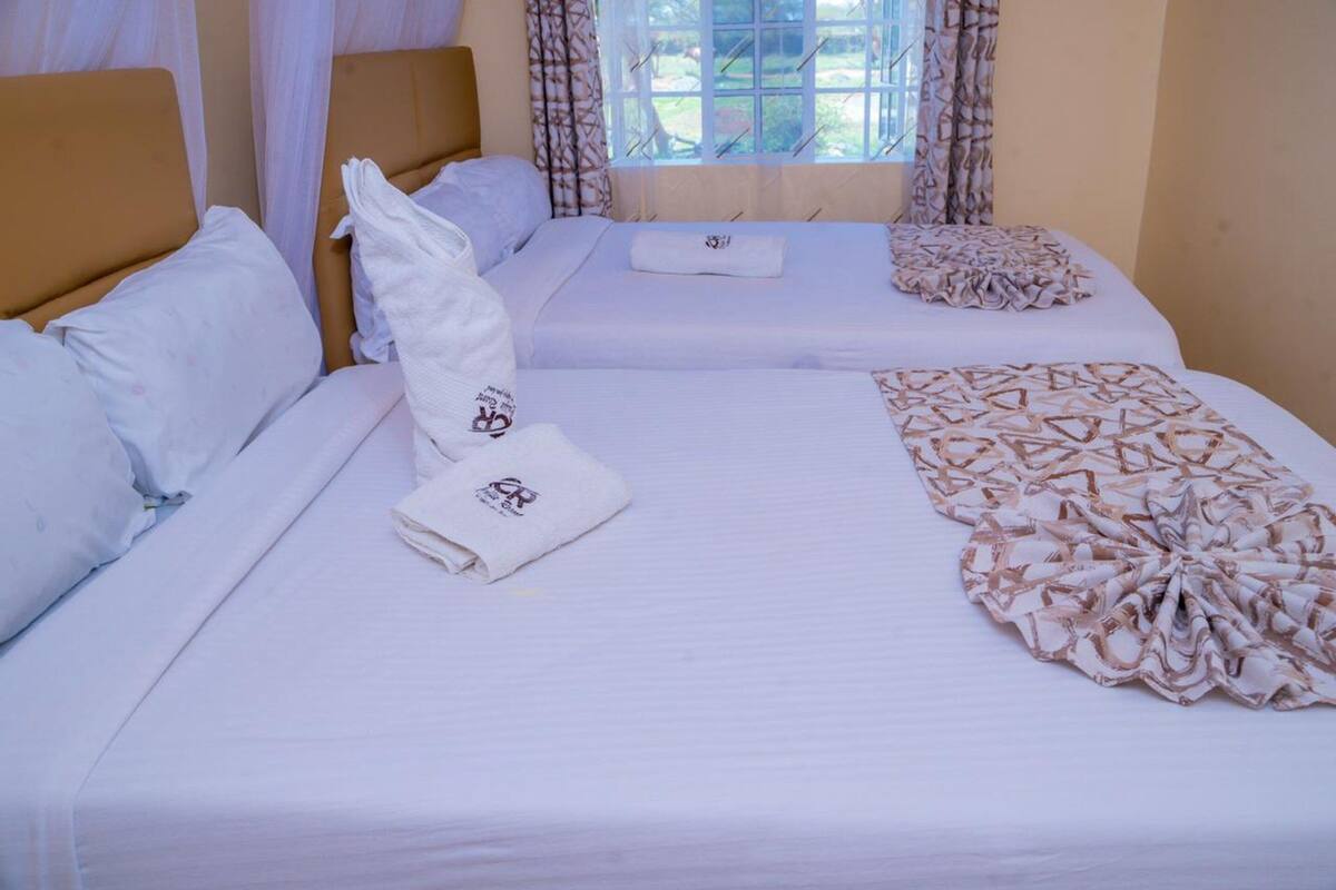 Quarto de hotel com duas camas, cada uma com lençóis brancos e almofadas decorativas.